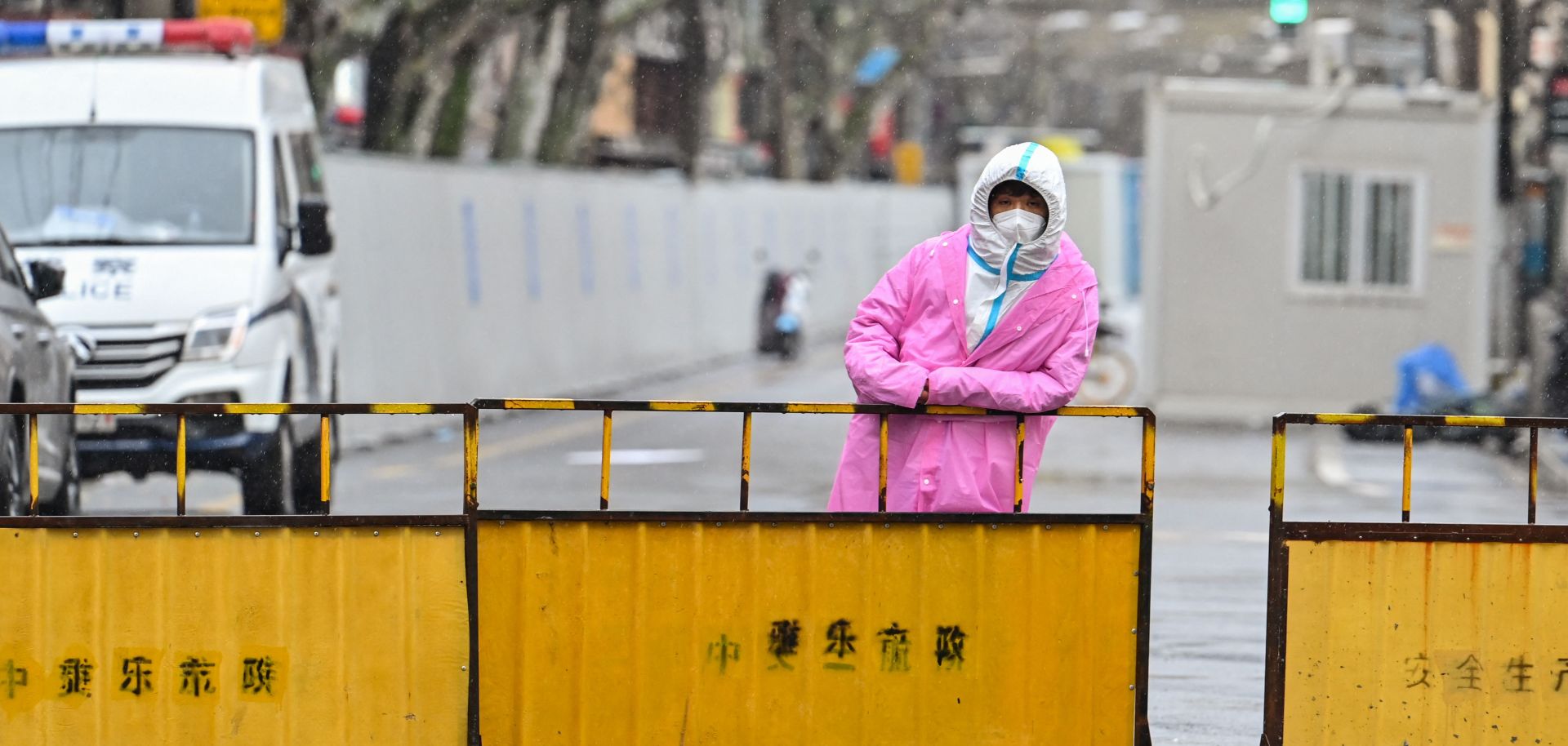 A worker wearing protective gear stands next to barriers placed to ...